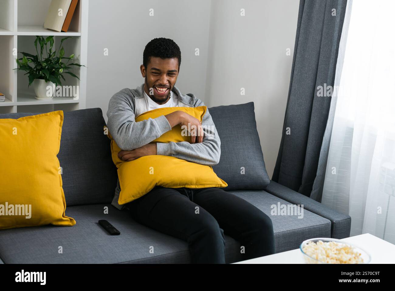 African american man focuses on the television while eating popcorn, fully immersed in show ...