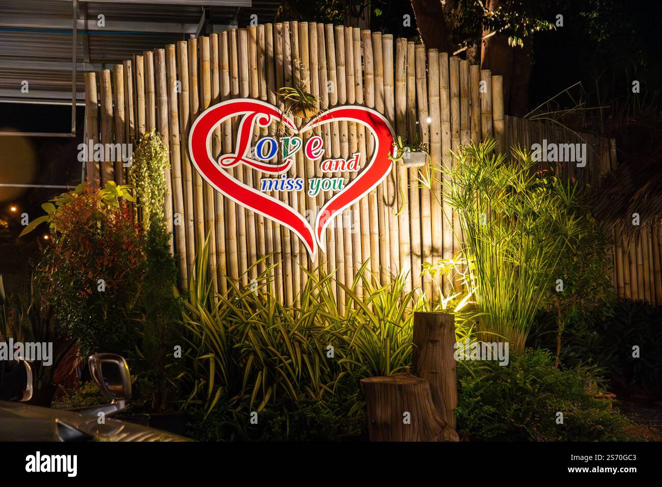 Neon love sign illuminated at night amidst lush greenery in an outdoor ...