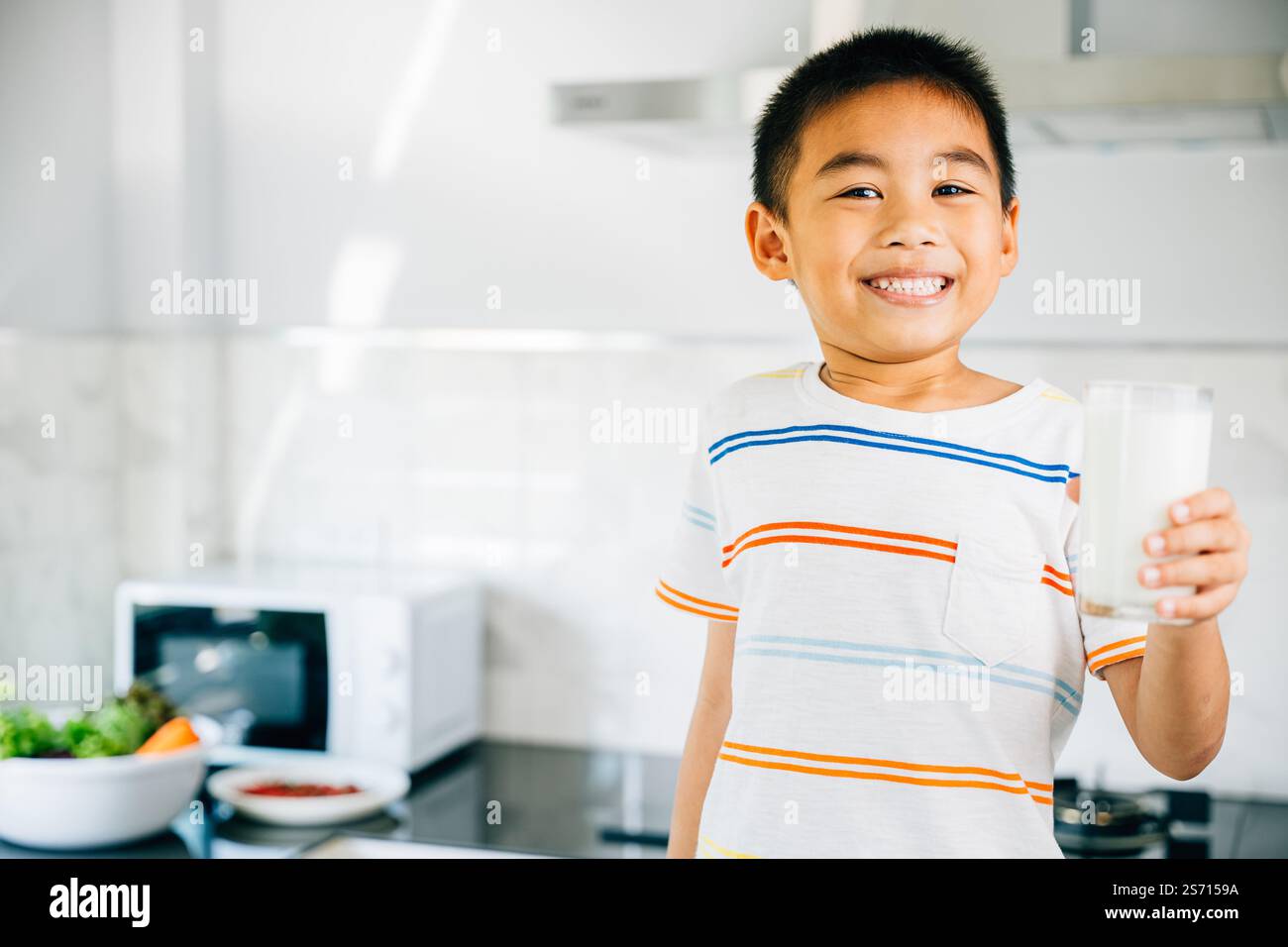 Portrait of happy Asian preschooler, boy holding milk in kitchen ...