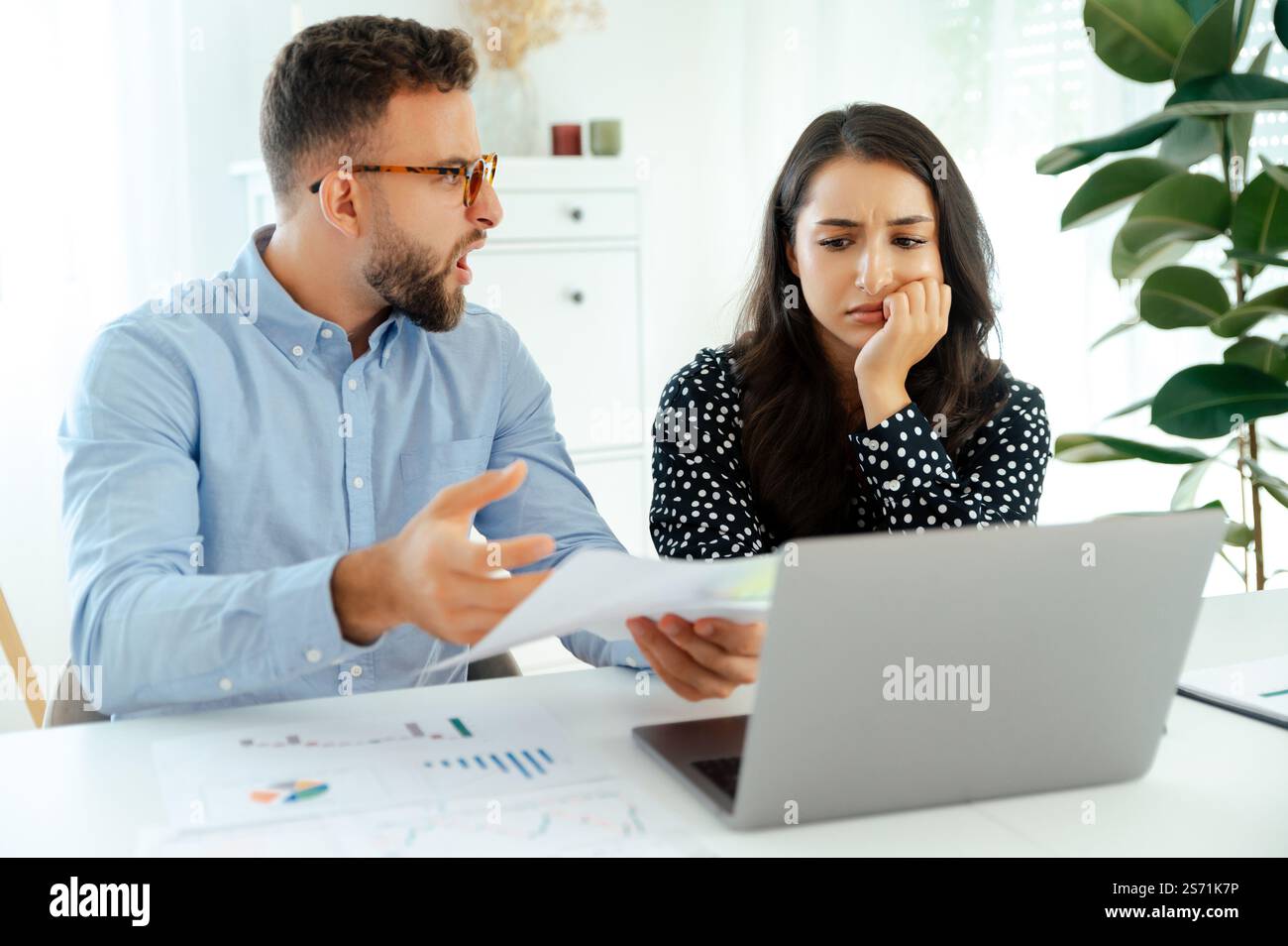 Frustrated irritated man holding printed charts speaking to a confused ...