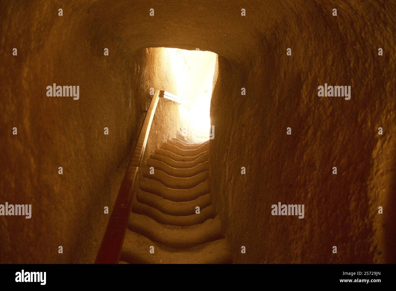 Ancient narrow tunnel with a carved stairway illuminated by sunlight ...