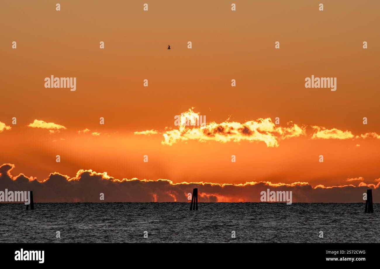 Fiery winter sunset taken with telephoto lens from the beach of Grado (Italy), intense colors ...