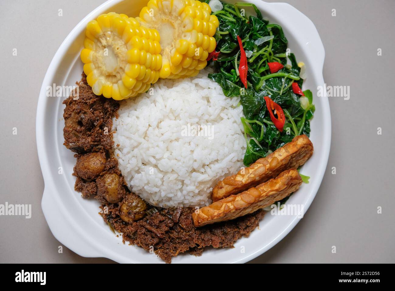 Indonesian homemade food, rice with rendang, fried tempeh, corn and ...