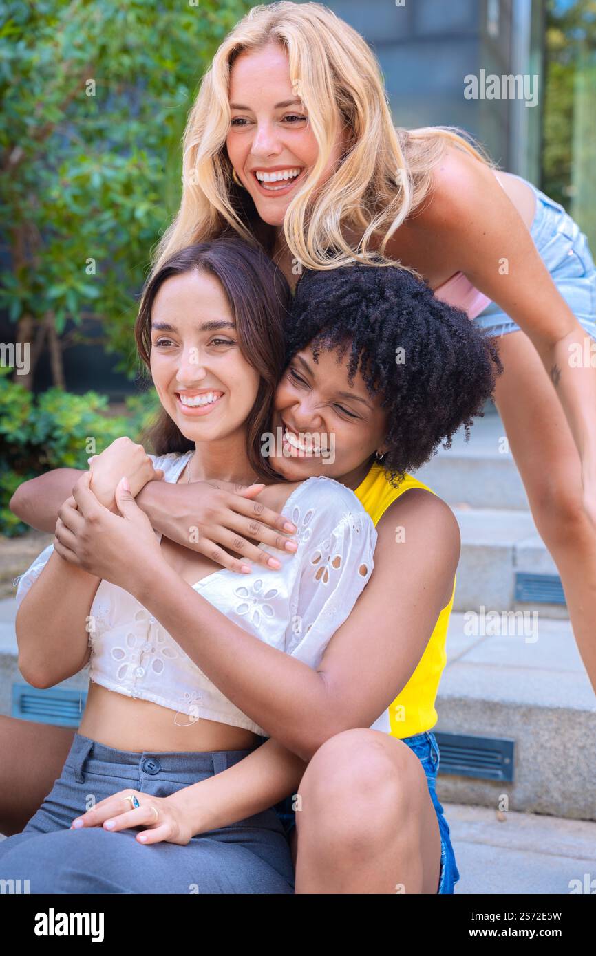 Three happy young women hugging and laughing together outdoors.Vertical ...