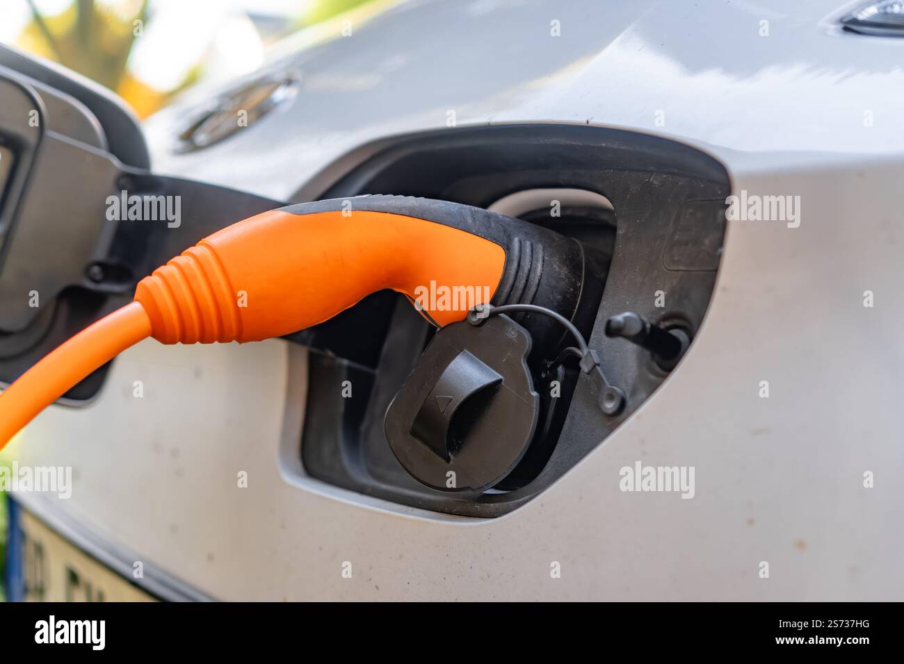 A car is being charged at a charging station. The orange handle of the ...