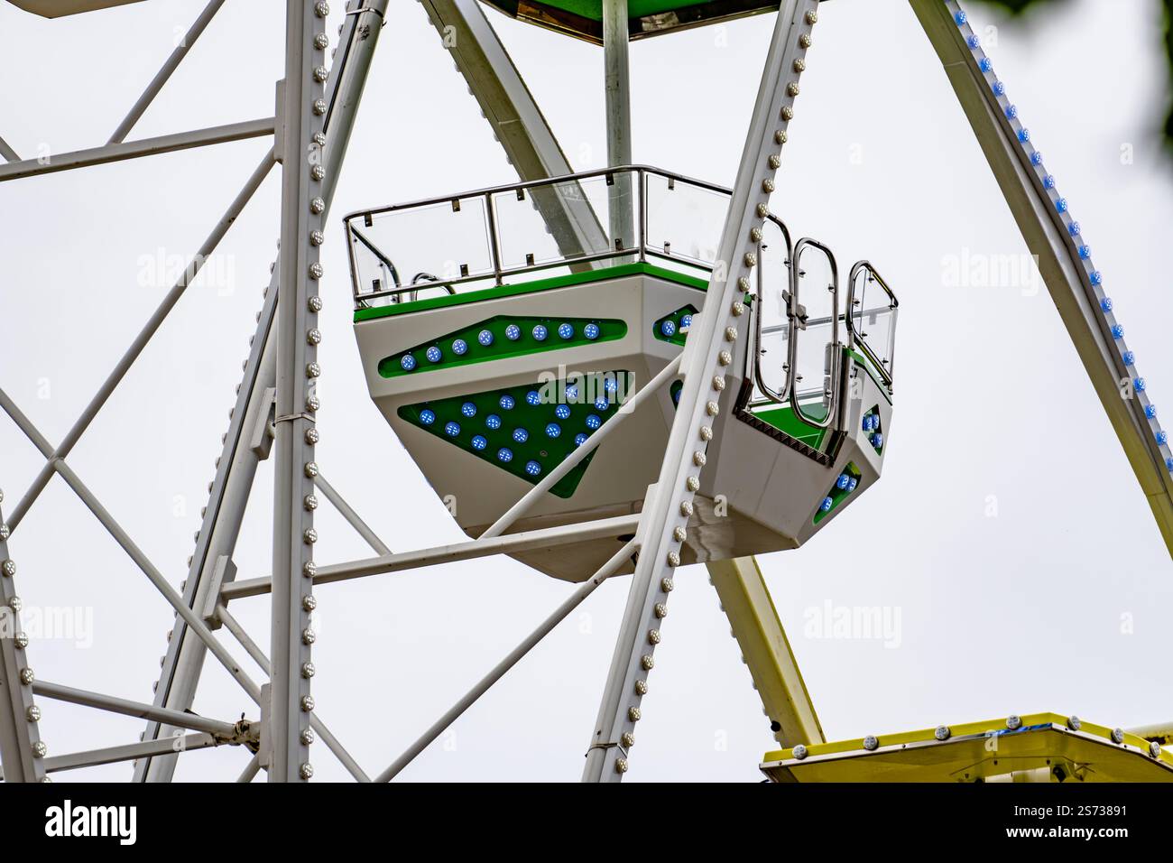 A Ferris wheel with a green and white seat. The seat is lit up with ...