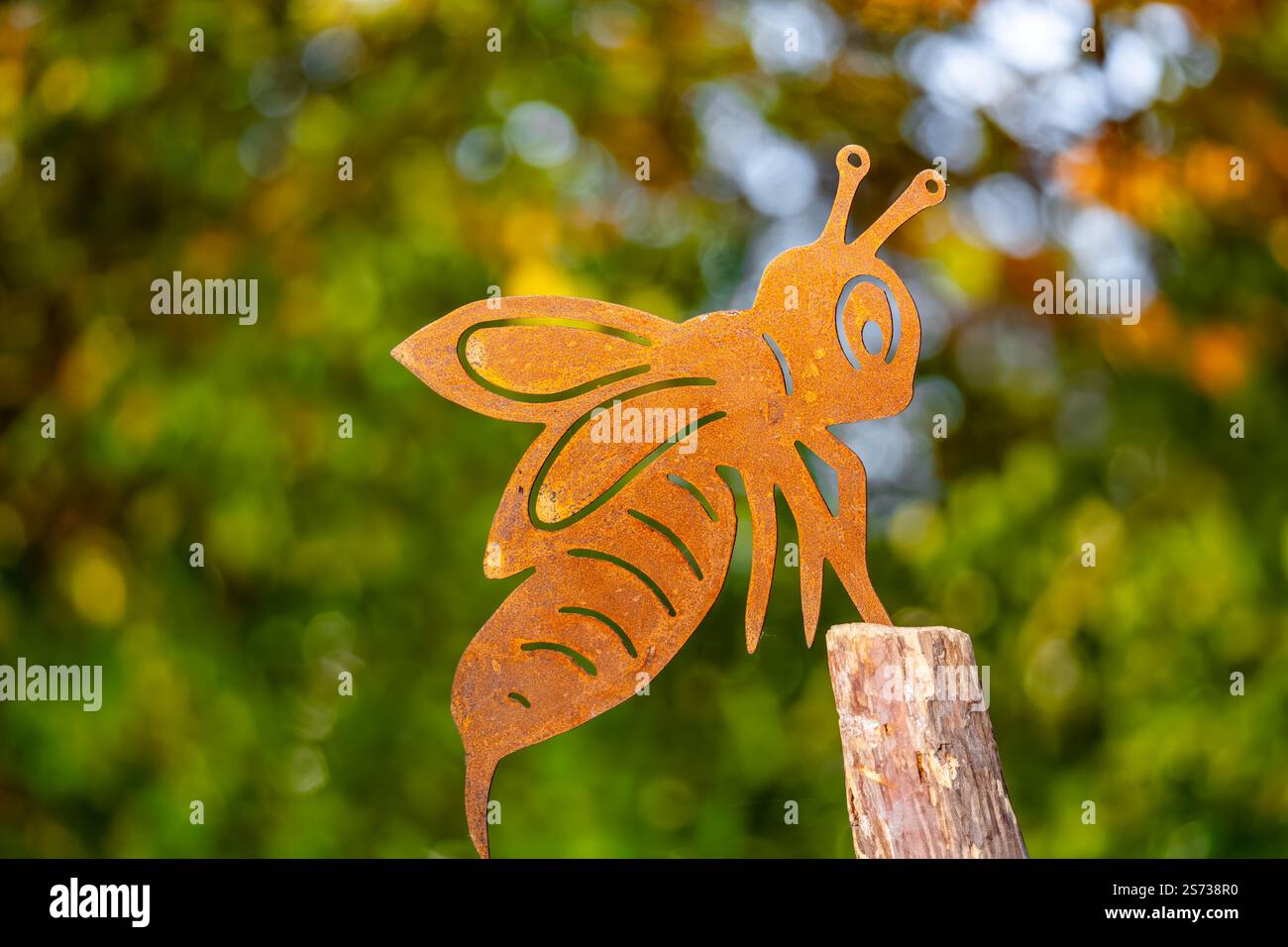 A metal sculpture of a bee is sitting on a wooden post. The sculpture ...