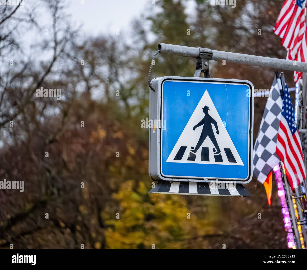 A pedestrian crossing sign is hanging from a pole. The sign is blue and ...