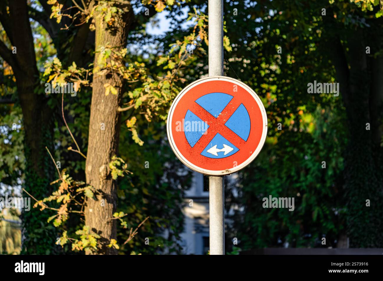 A red and blue sign with a white X on it is on a pole. The sign is in a ...