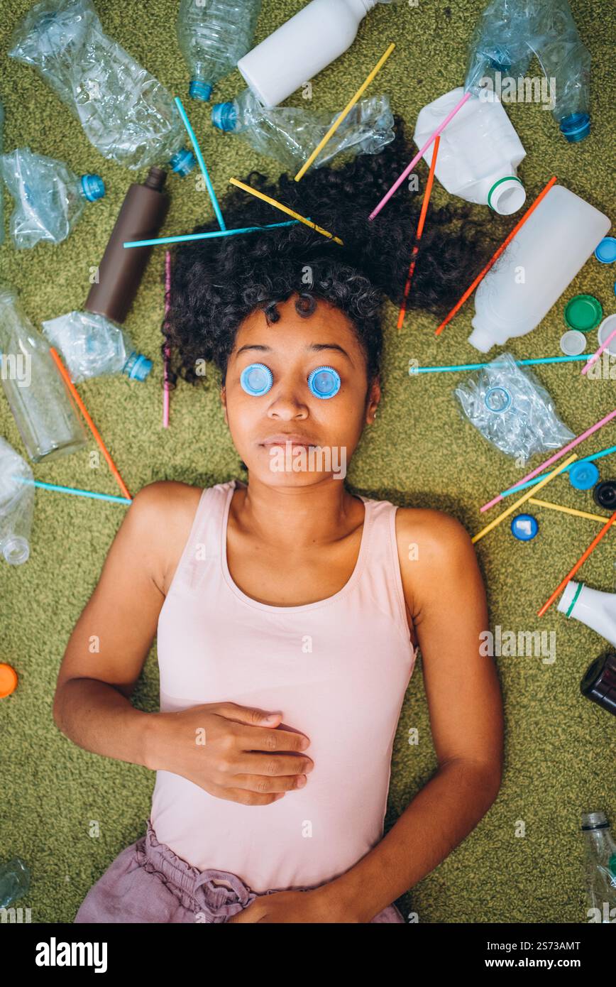 Young woman lying on a green carpet covered with plastic trash, straws ...