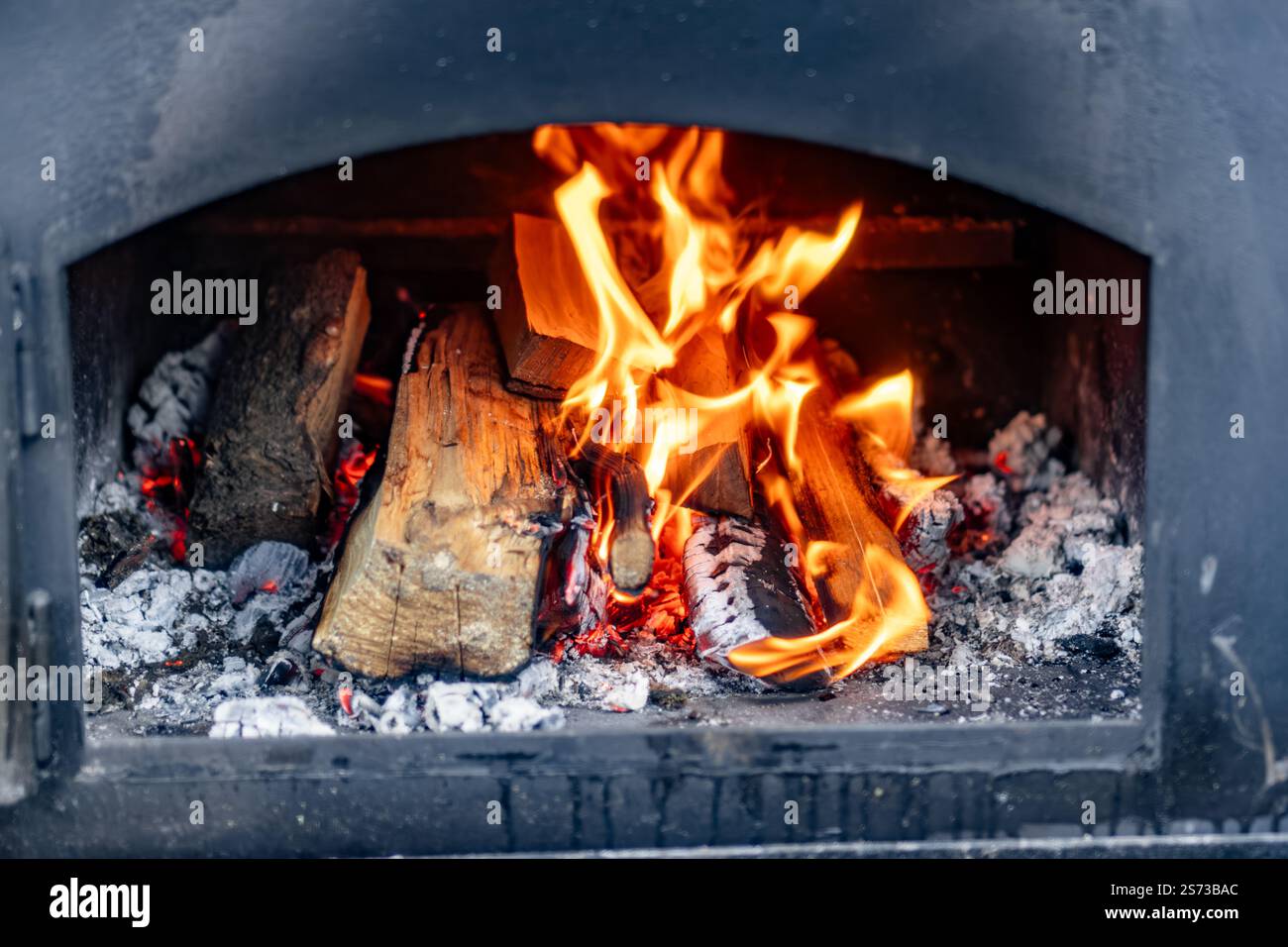 A wood burning fire in a black oven. The fire is very hot and the wood ...