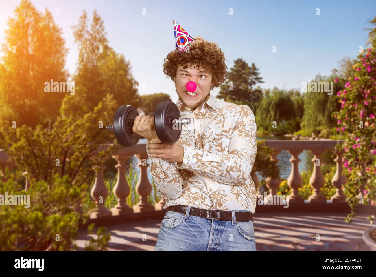 Portrait of a young clown making funny face and holding a dumbbell ...