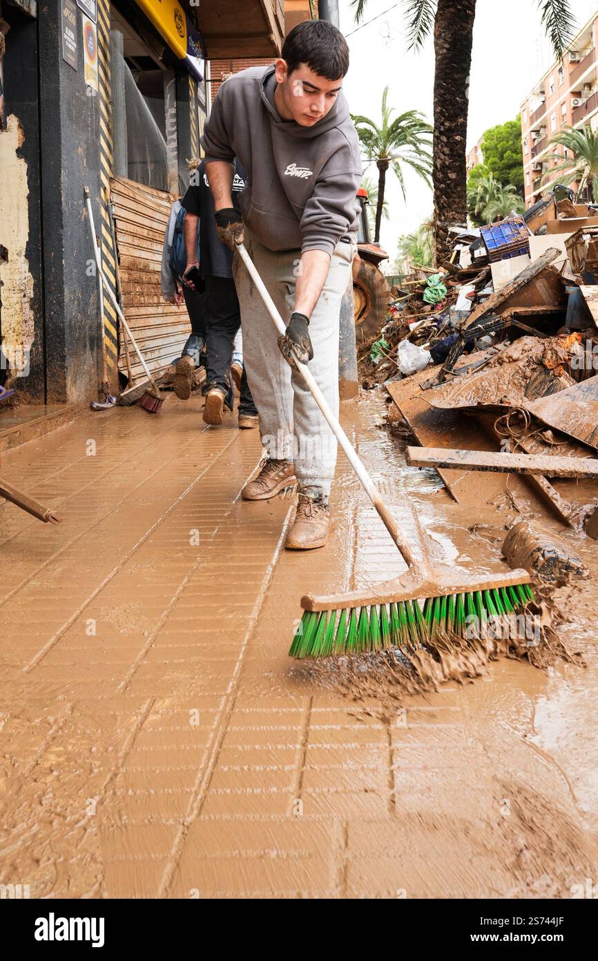 Young man with sweeper brush sweeping mud from the sidewalk with debris ...