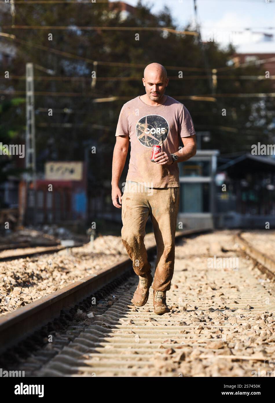 Bald athletic man covered in mud walking on a railway track with a Coca ...