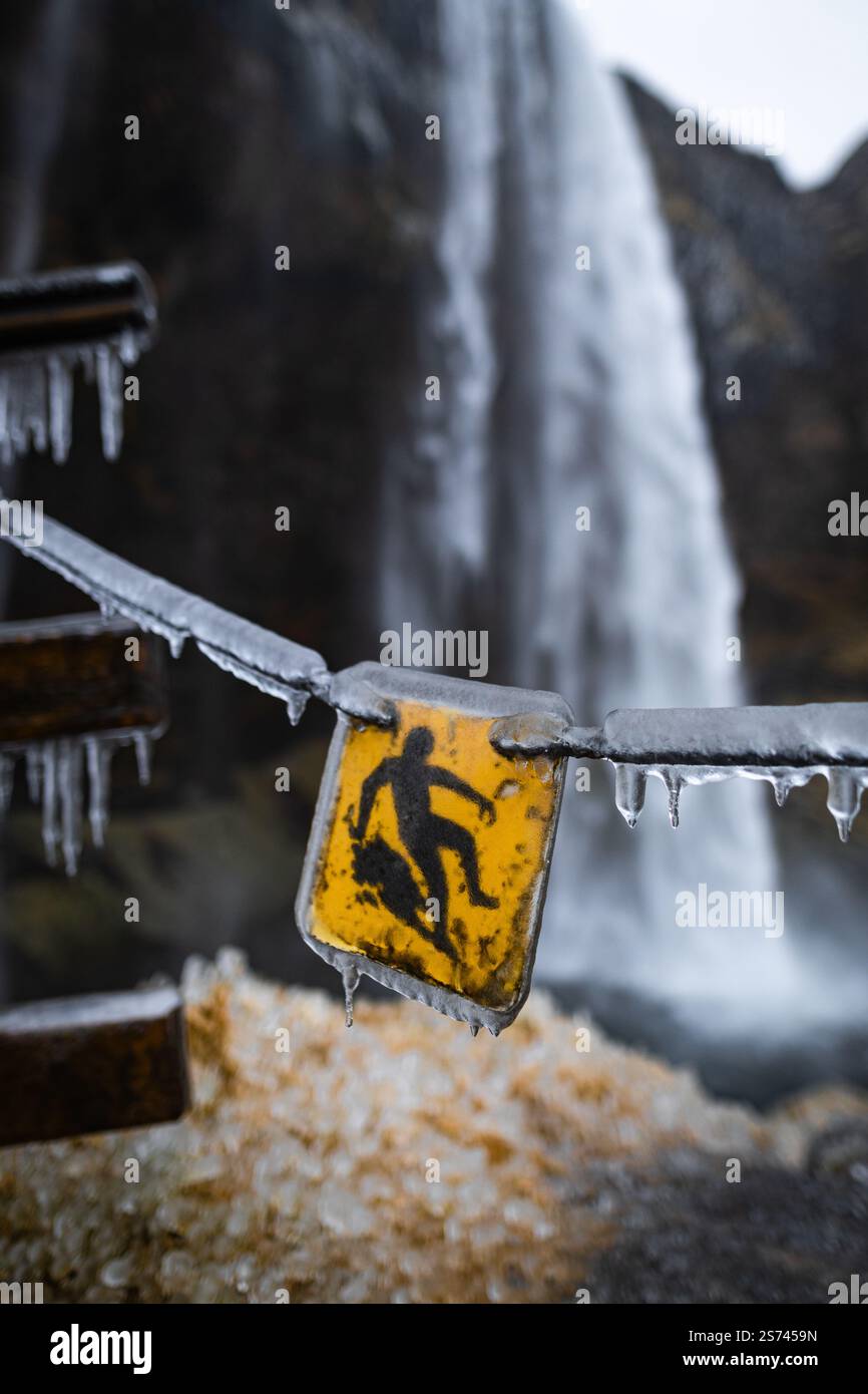 A frozen warning sign hangs from a railing beside a waterfall ...