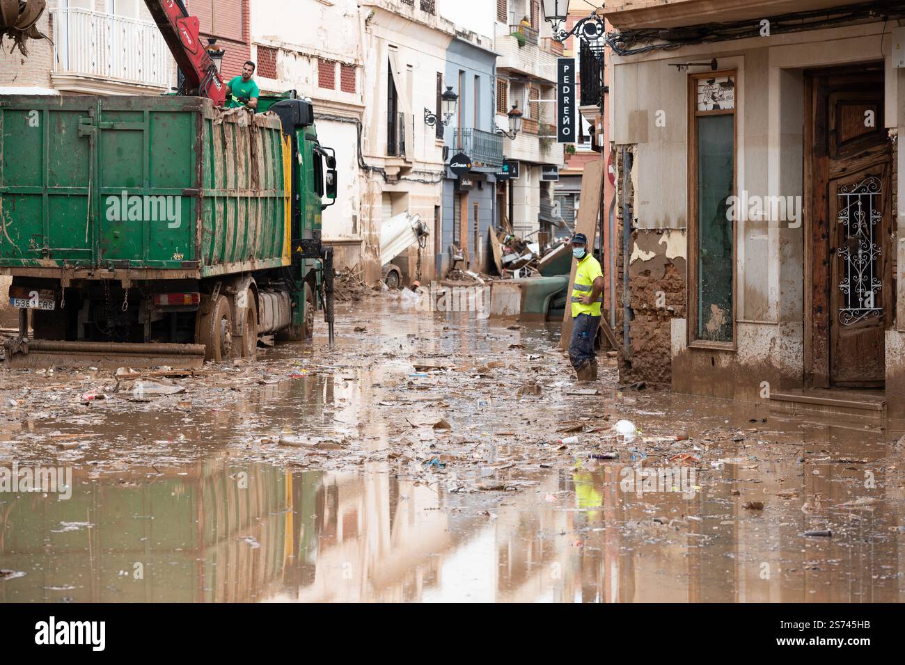 Man sinking in muddy street with furniture and debris piles and worker ...