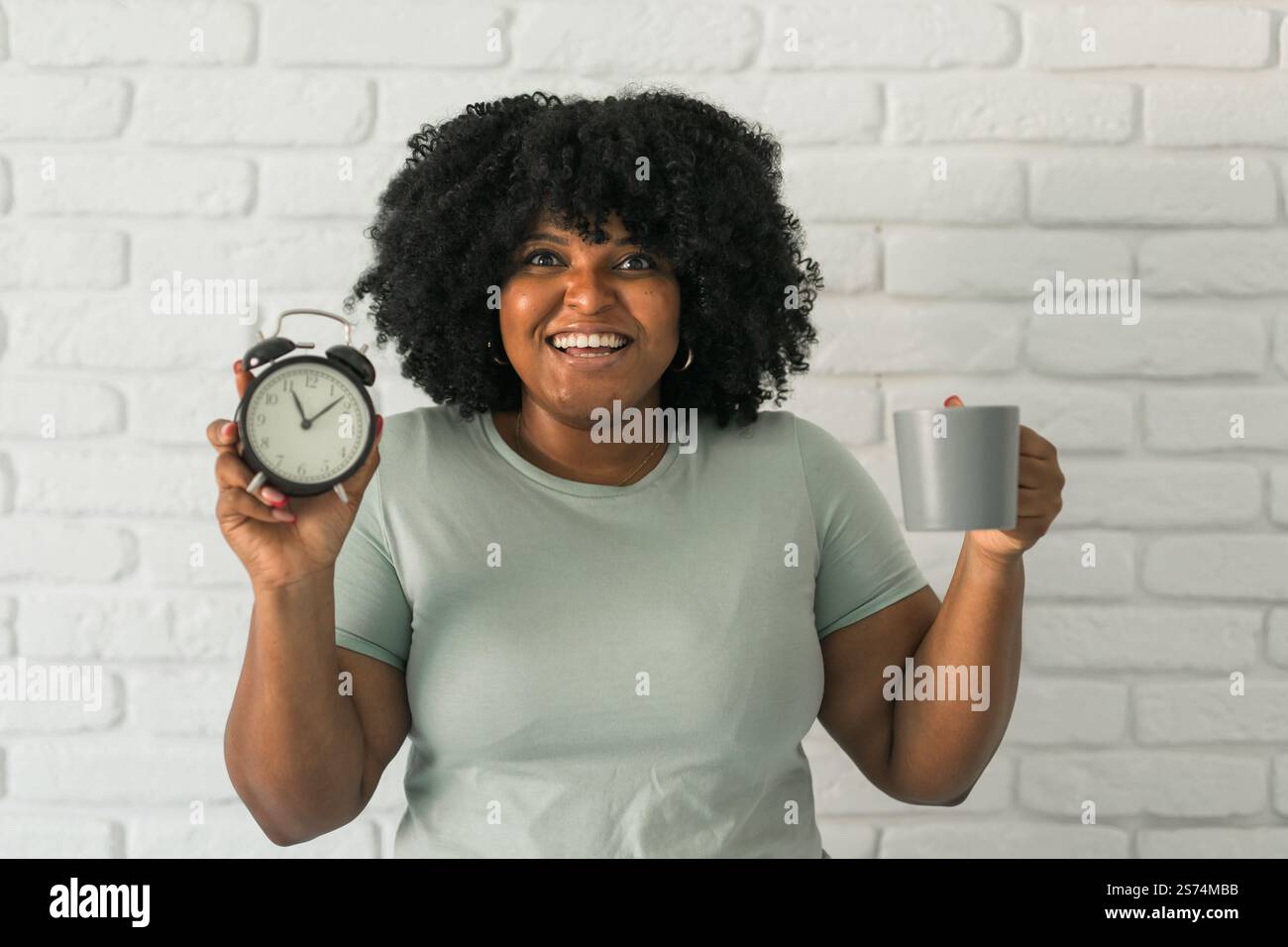 Happy african american woman holding alarm clock amazed with open mouth ...