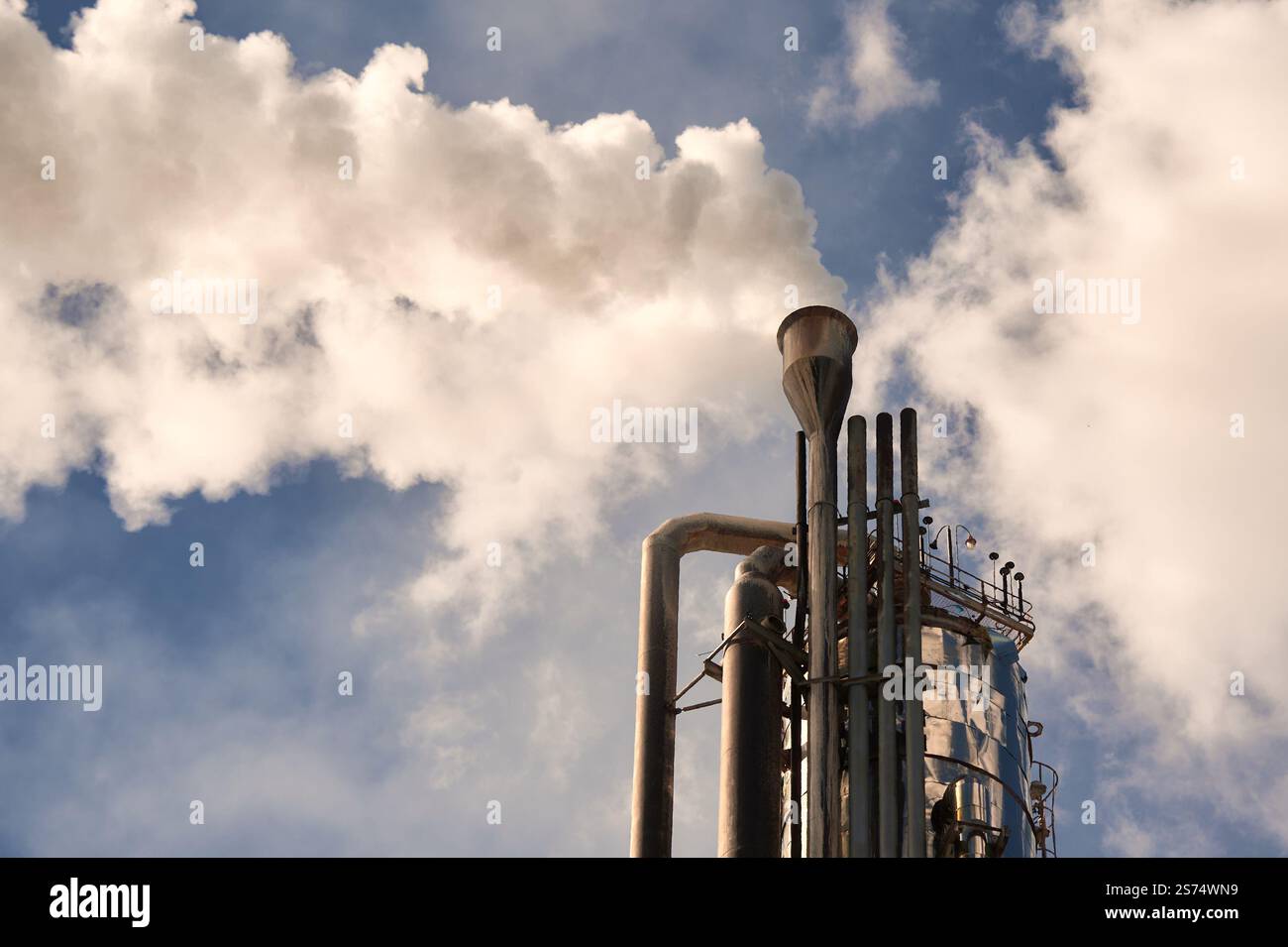 A distillation column releases steam in a chemical plant under a clear ...
