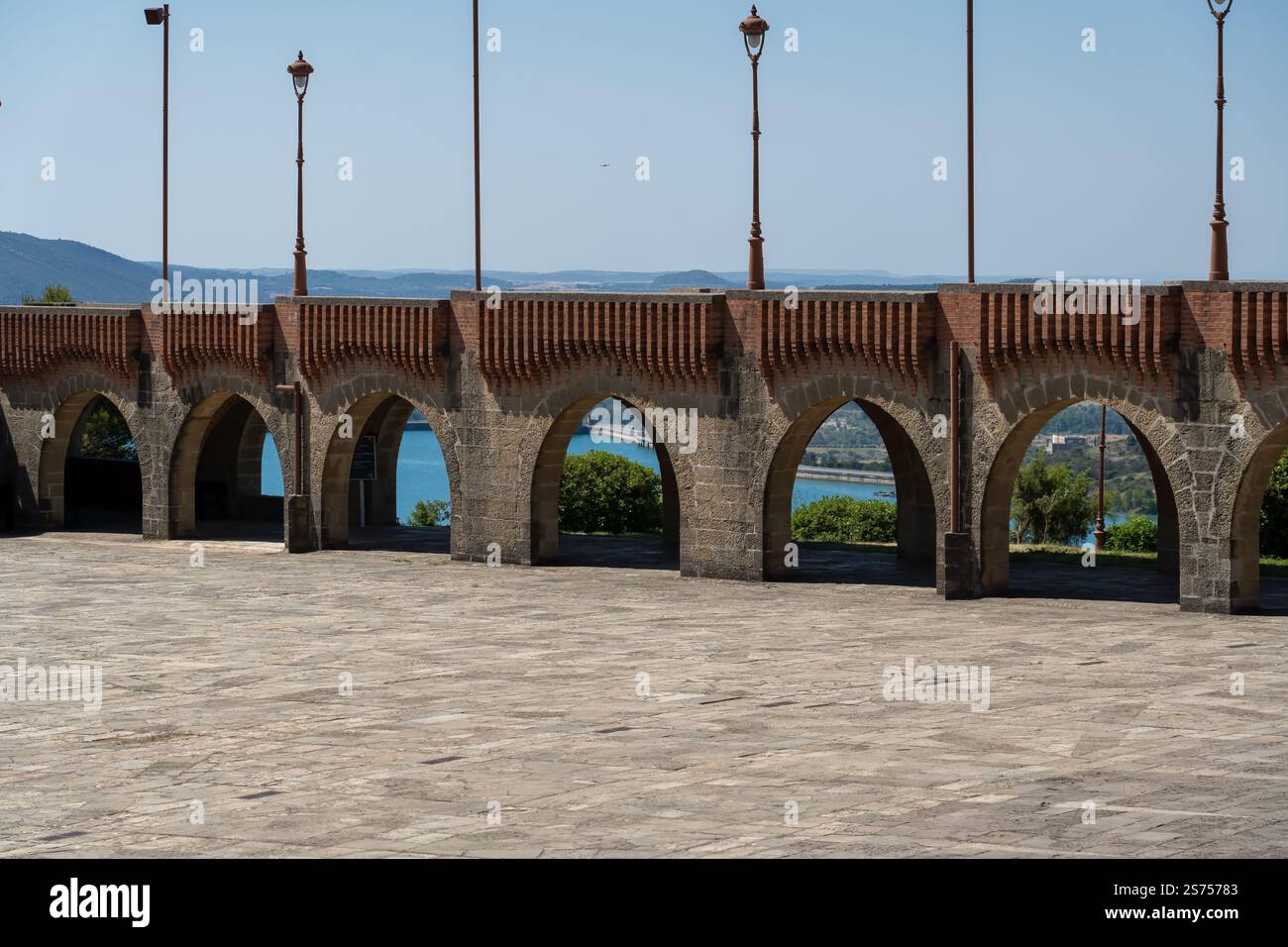red brick romanesque archways with blue reservoir water beyond ...