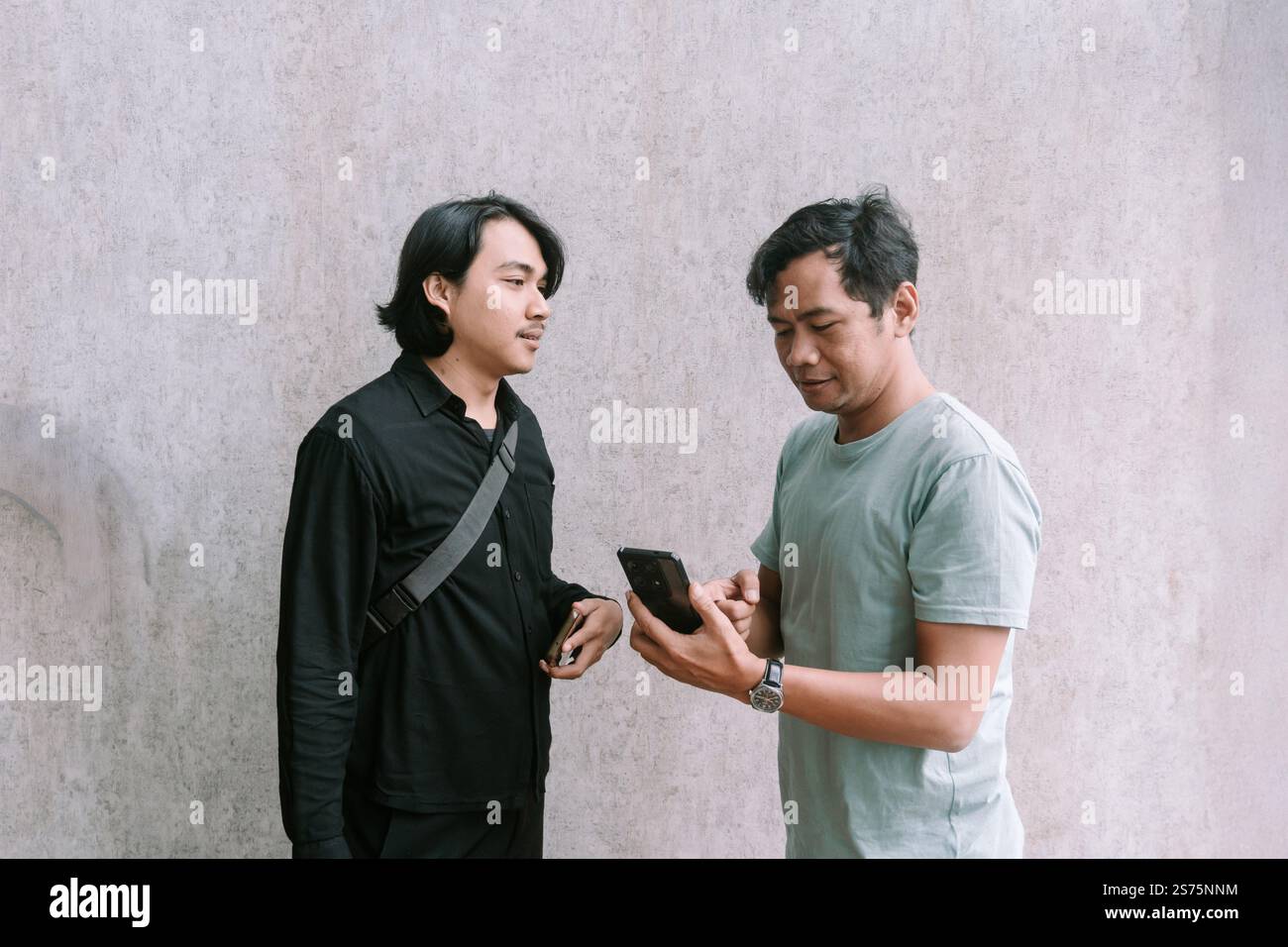 Two men engage in a conversation while looking at a mobile phone ...