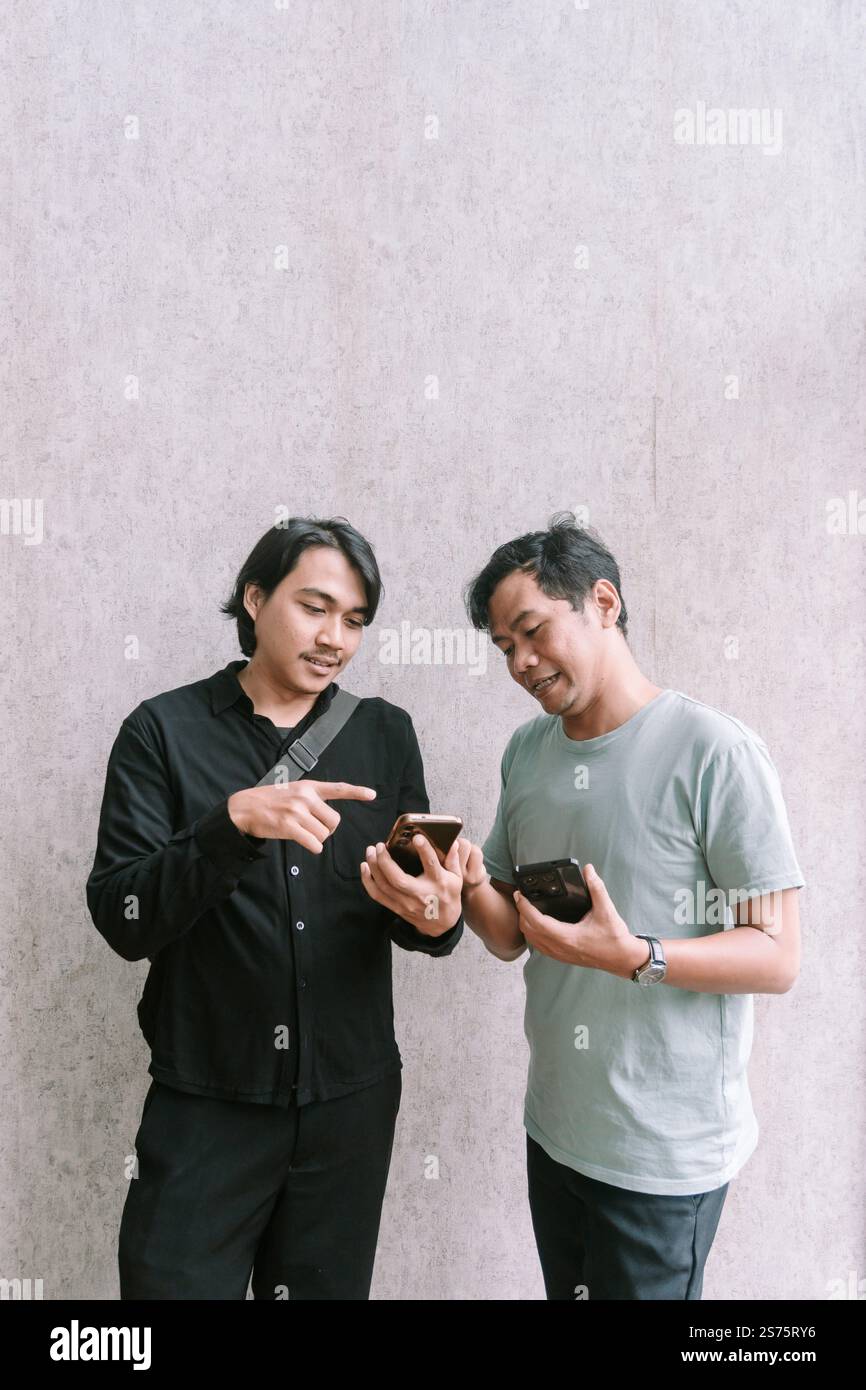 A man points at a mobile phone screen, sharing content with his friend ...