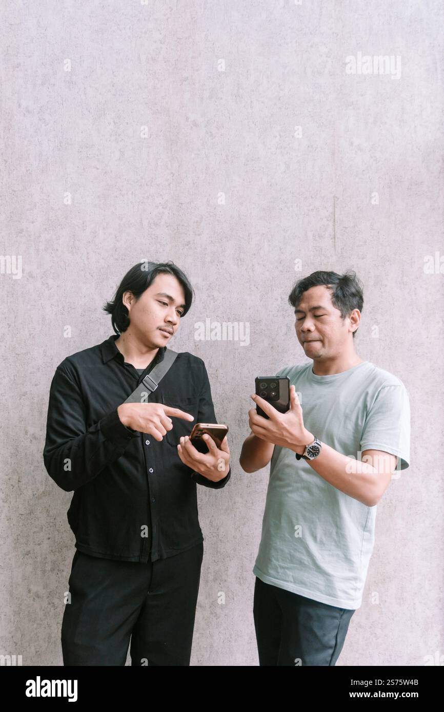 A man points at a mobile phone screen, sharing content with his friend ...