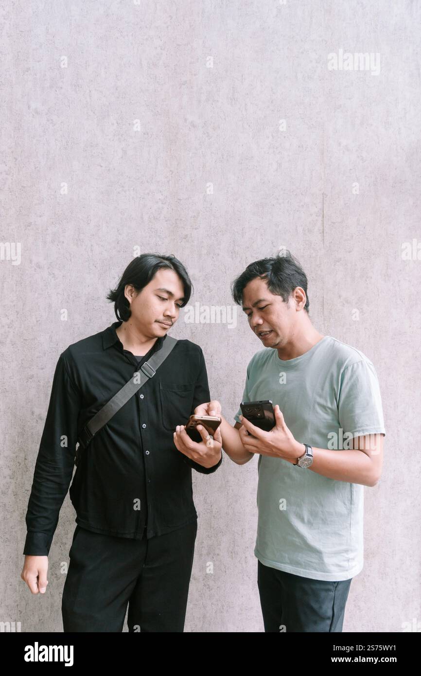 A man points at a mobile phone screen, sharing content with his friend ...