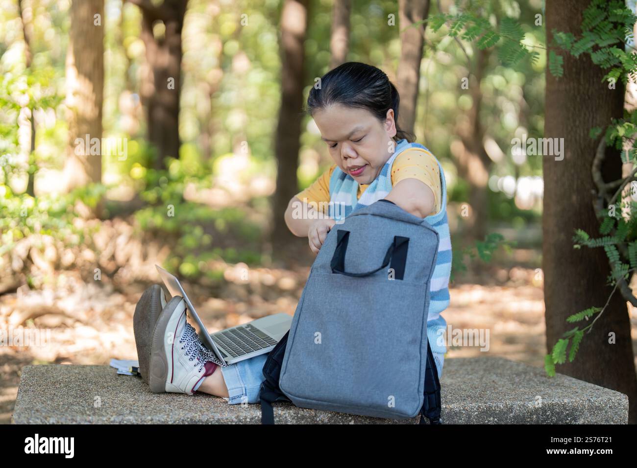 Woman with achondroplasia organizing her backpack while using a laptop ...