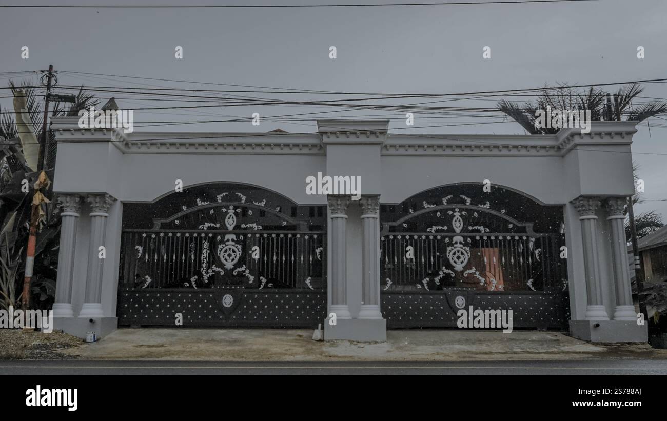 A grand entrance gate with ornate black metalwork and white columns ...