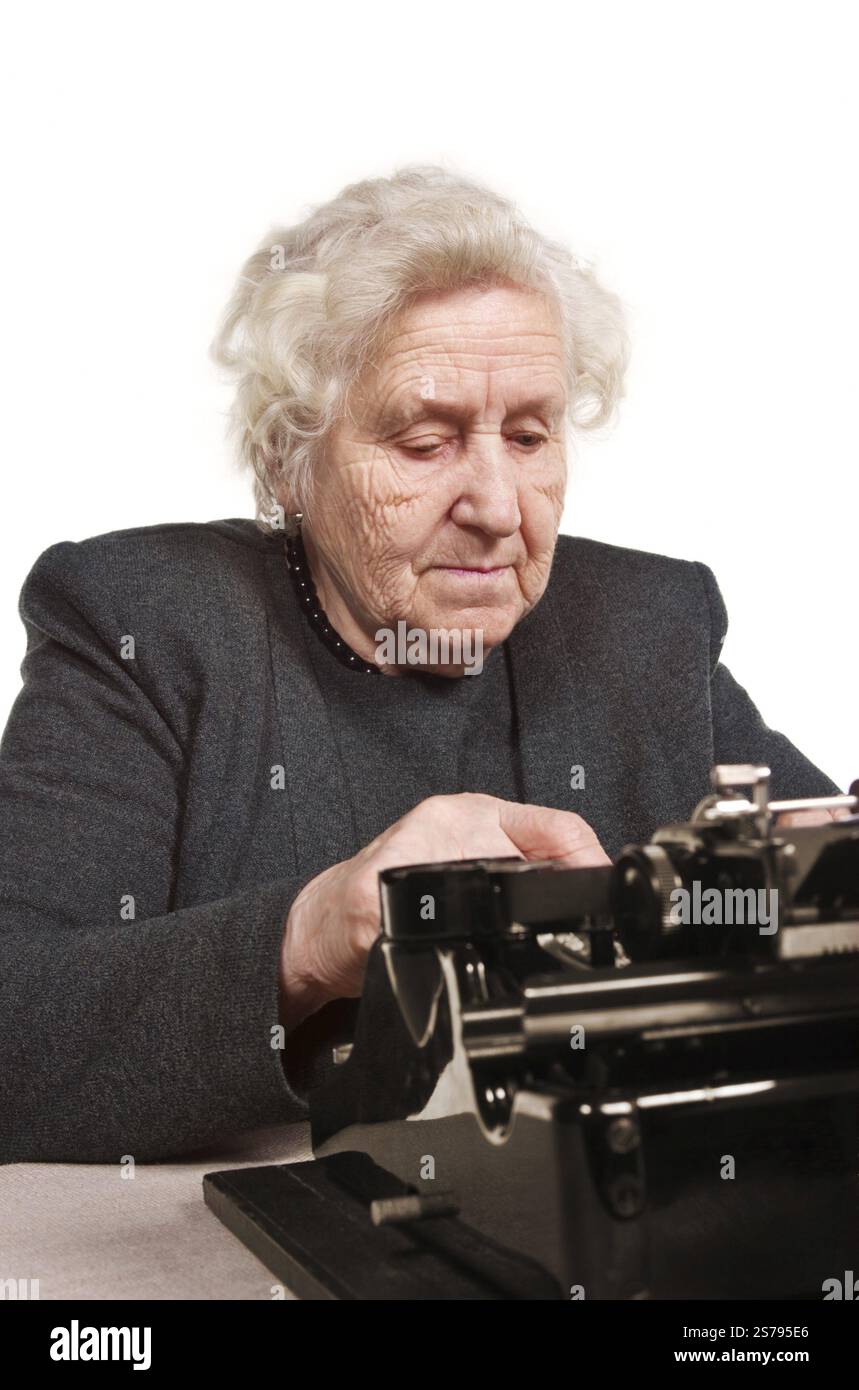 Old woman typing on an old-fashioned typewriter against a white ...