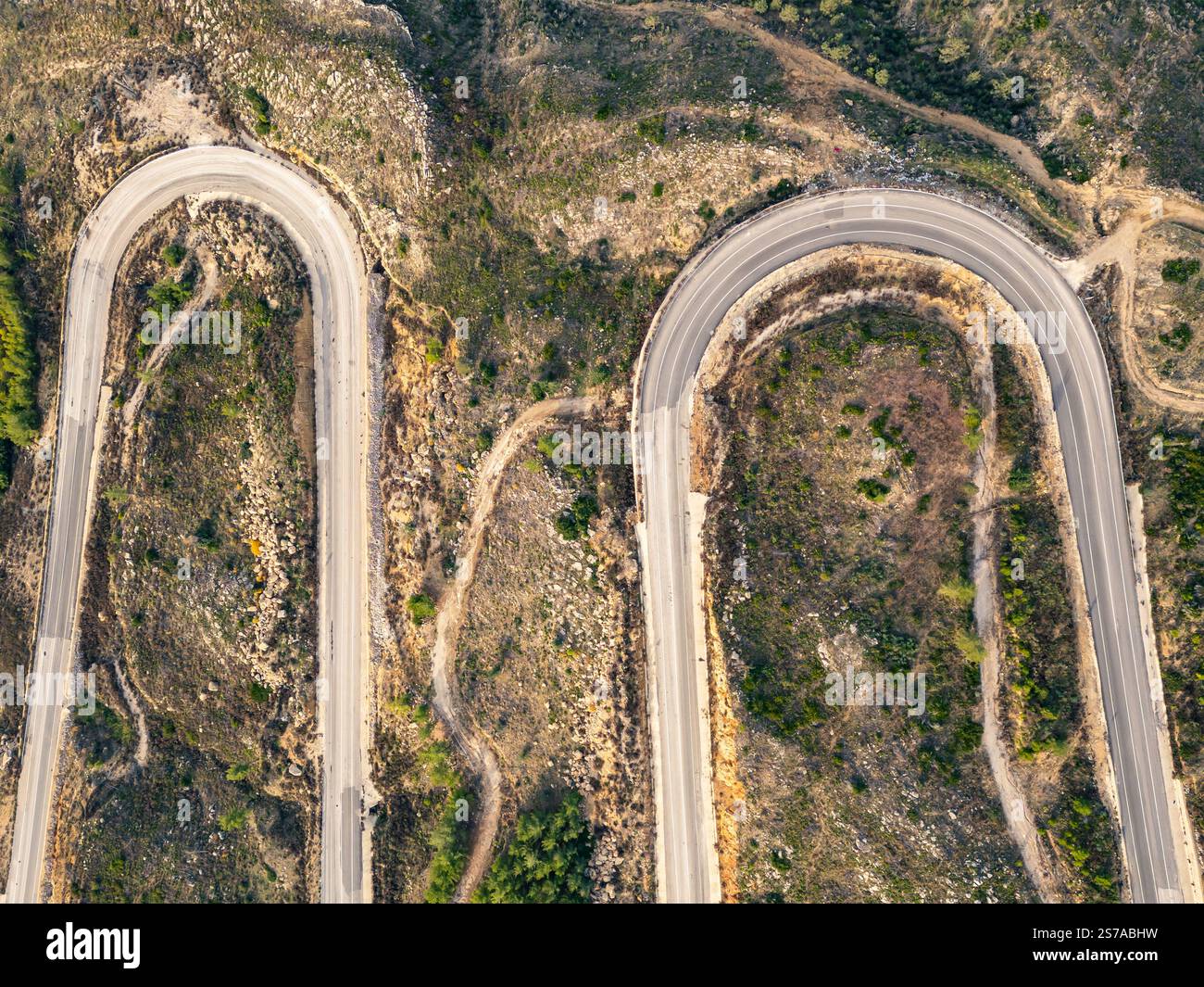 A winding asphalt road that passes through areas with few trees in ...