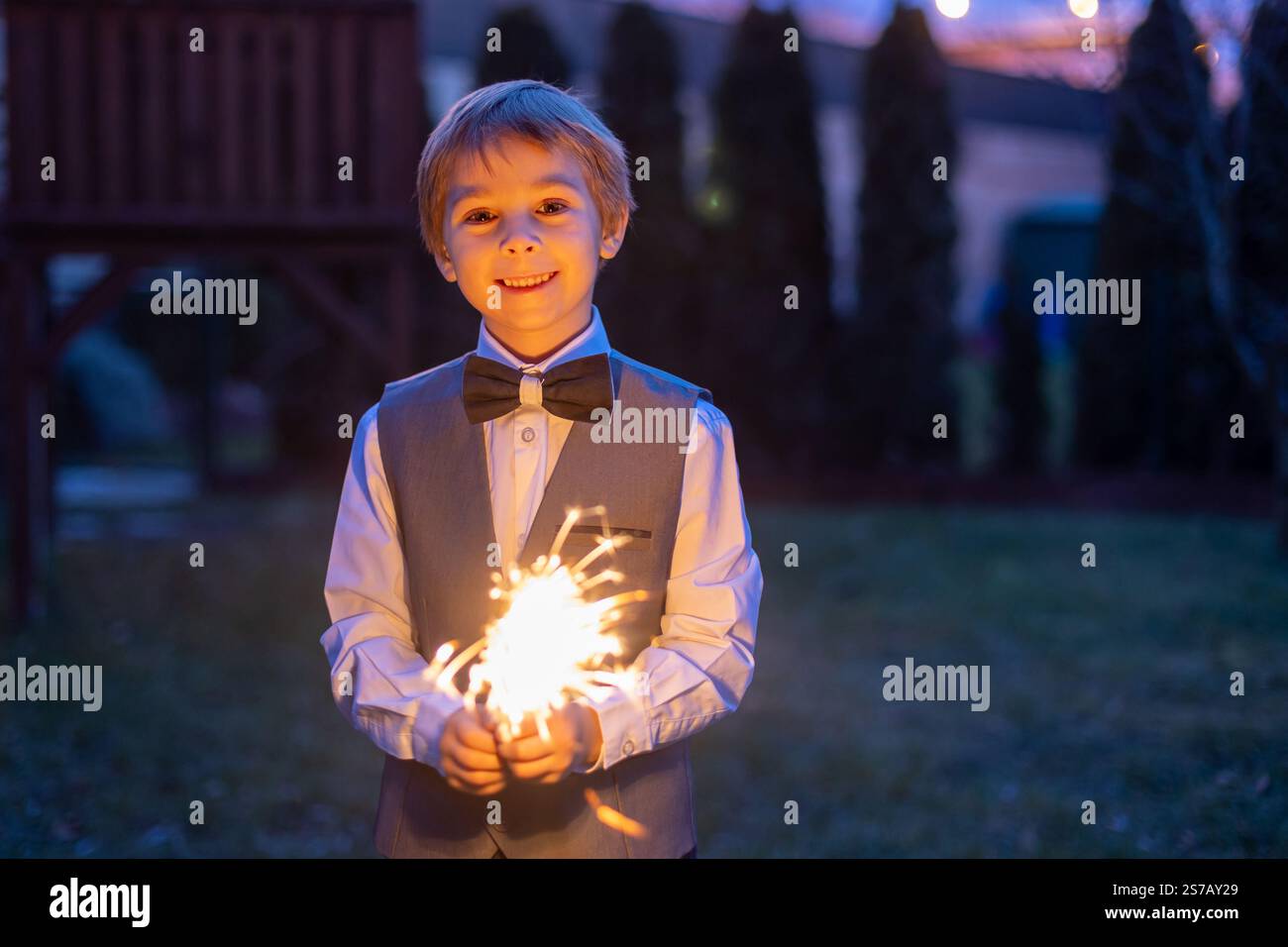 School child, boy on New Years Eve, holding sparkler in garden ...