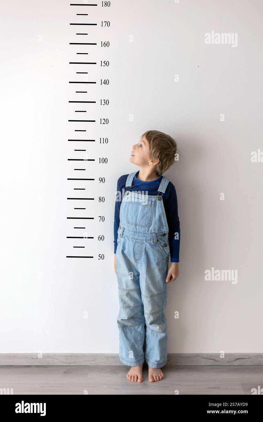 Little child, boy, measuring height against wall in room at home, white ...