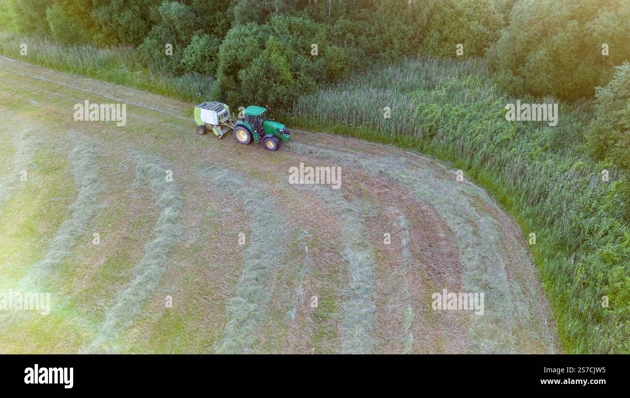 Aerial view of a tractor with a baler on a field, surrounded by trees ...