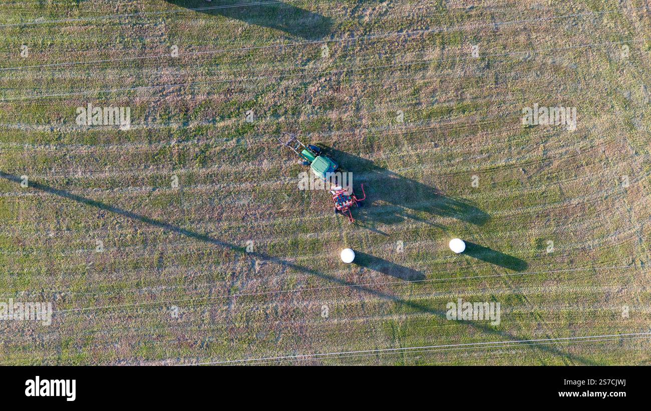 Aerial view of a field with tractor baling hay, with hay bales scattered across the landscape ...