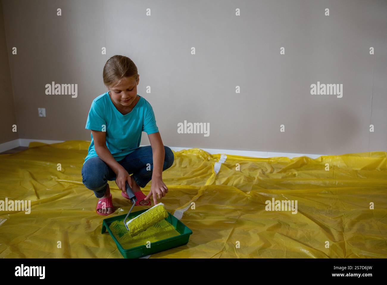 A young child joyfully painting a room using a roller and a paint tray ...