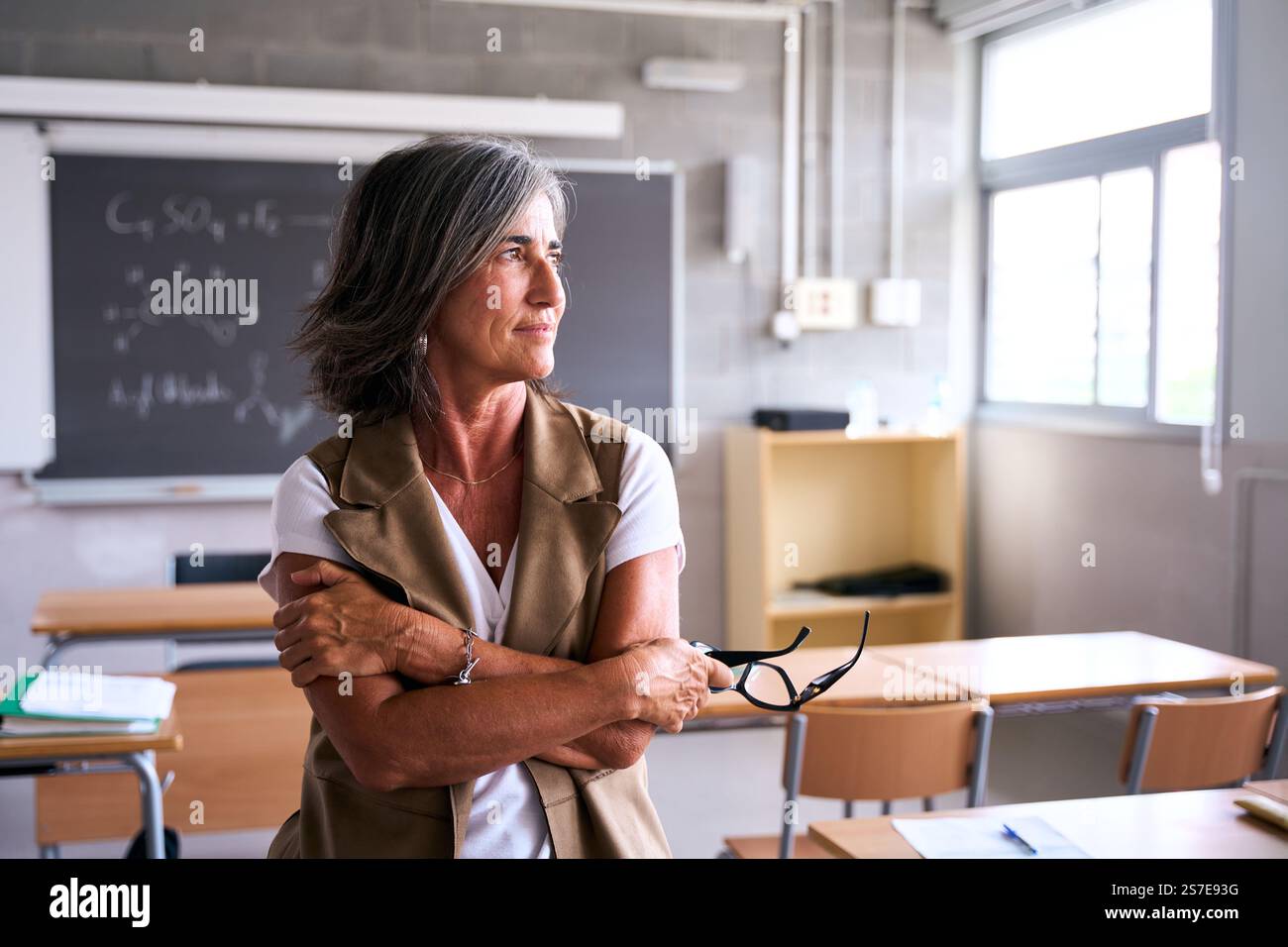 A teacher stands alone in an empty classroom, gazing thoughtfully out ...