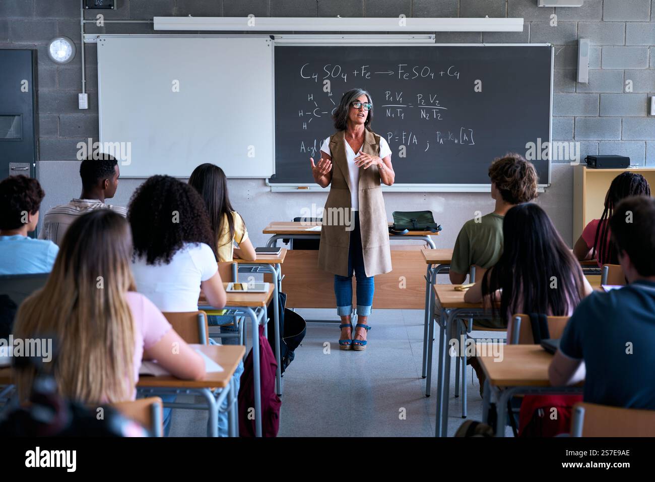 A teacher stands at the front of a classroom, giving a lesson to her ...