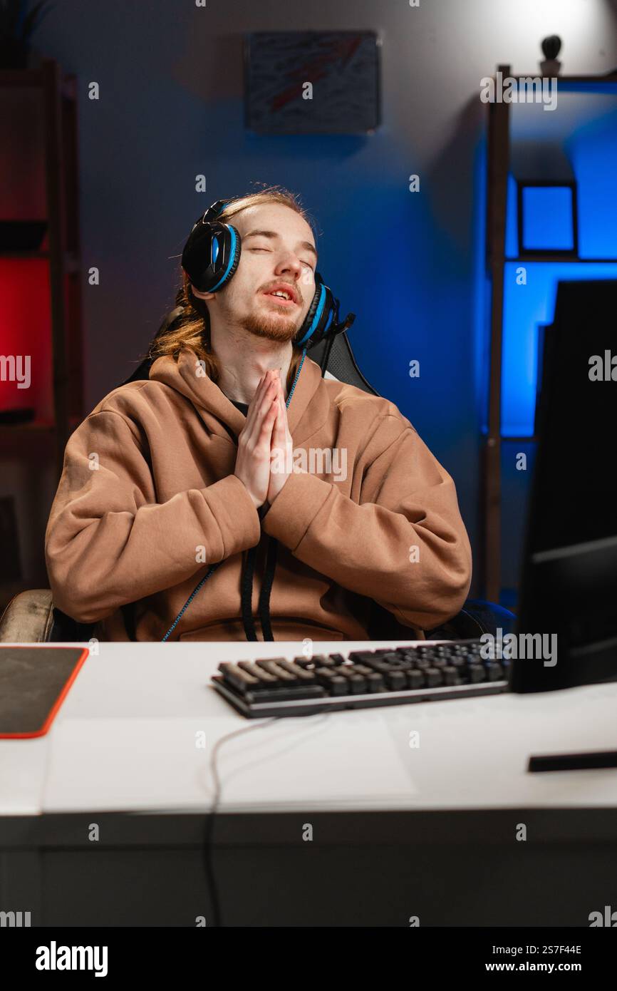 Male gamer wearing headphones playing video games praying with hands ...