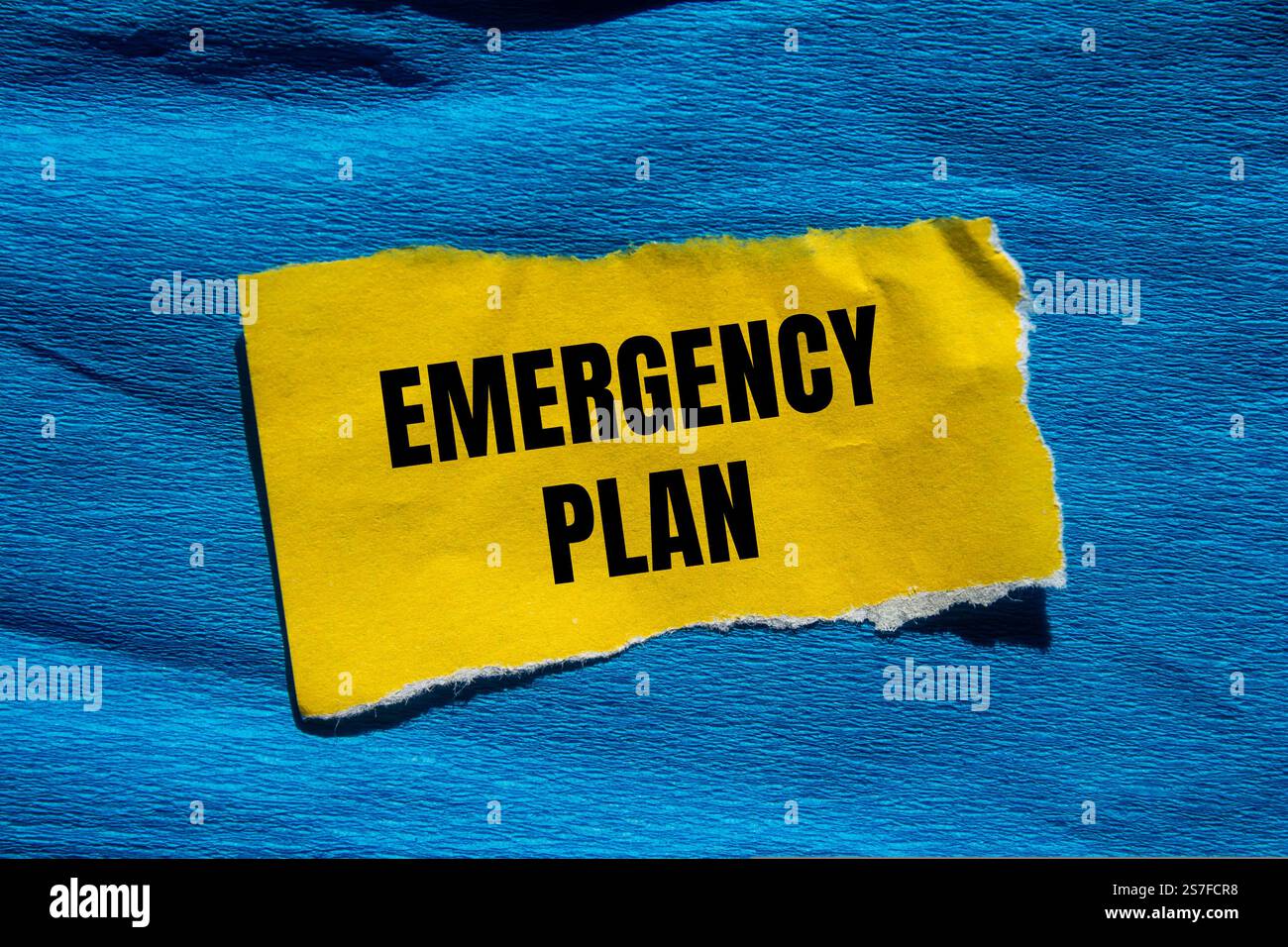 Emergency plan message written on ripped torn yellow paper piece with blue background ...