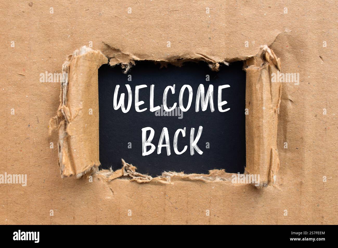 Welcome back message written on ripped torn cardboard paper with black background. Conceptual ...