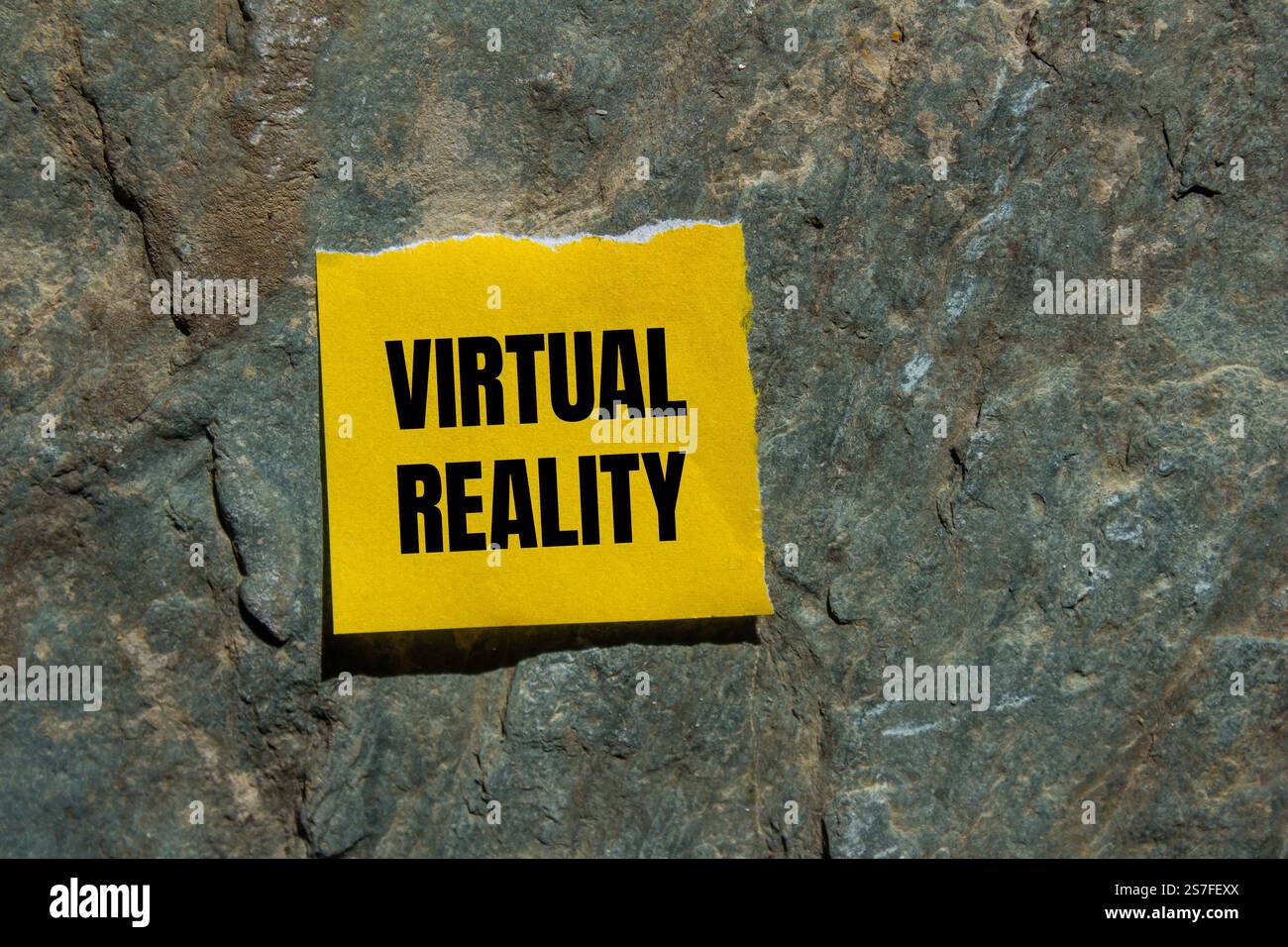 Virtual reality message written on ripped torn yellow paper piece with stone background ...