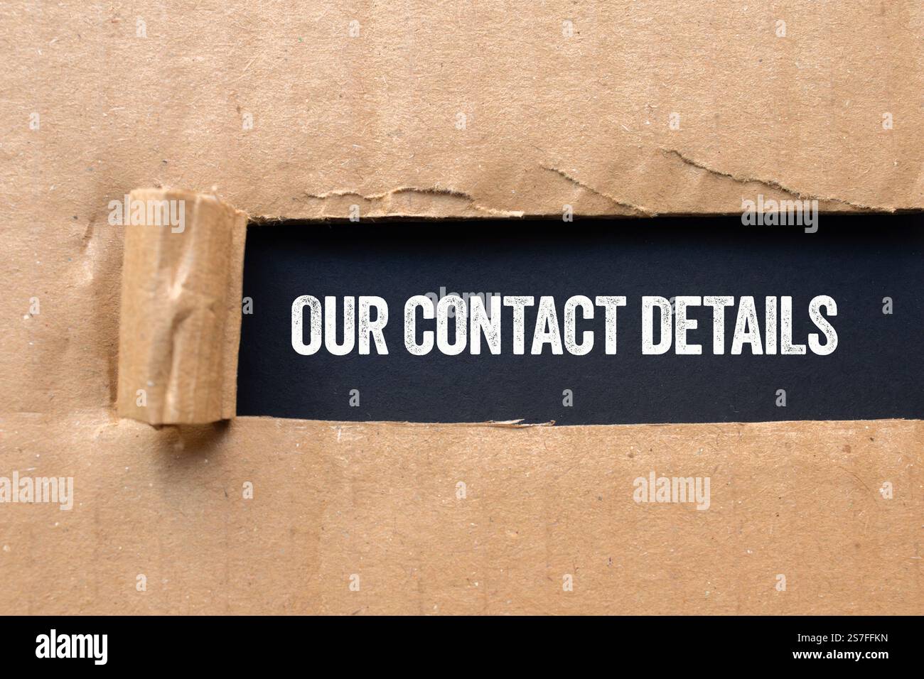 Our contact details message written on ripped torn cardboard paper on black background ...