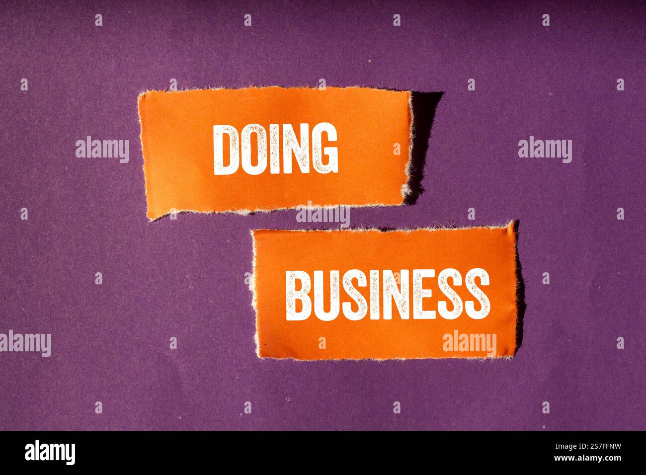 Doing business message written on ripped torn orange paper pieces on purple background ...