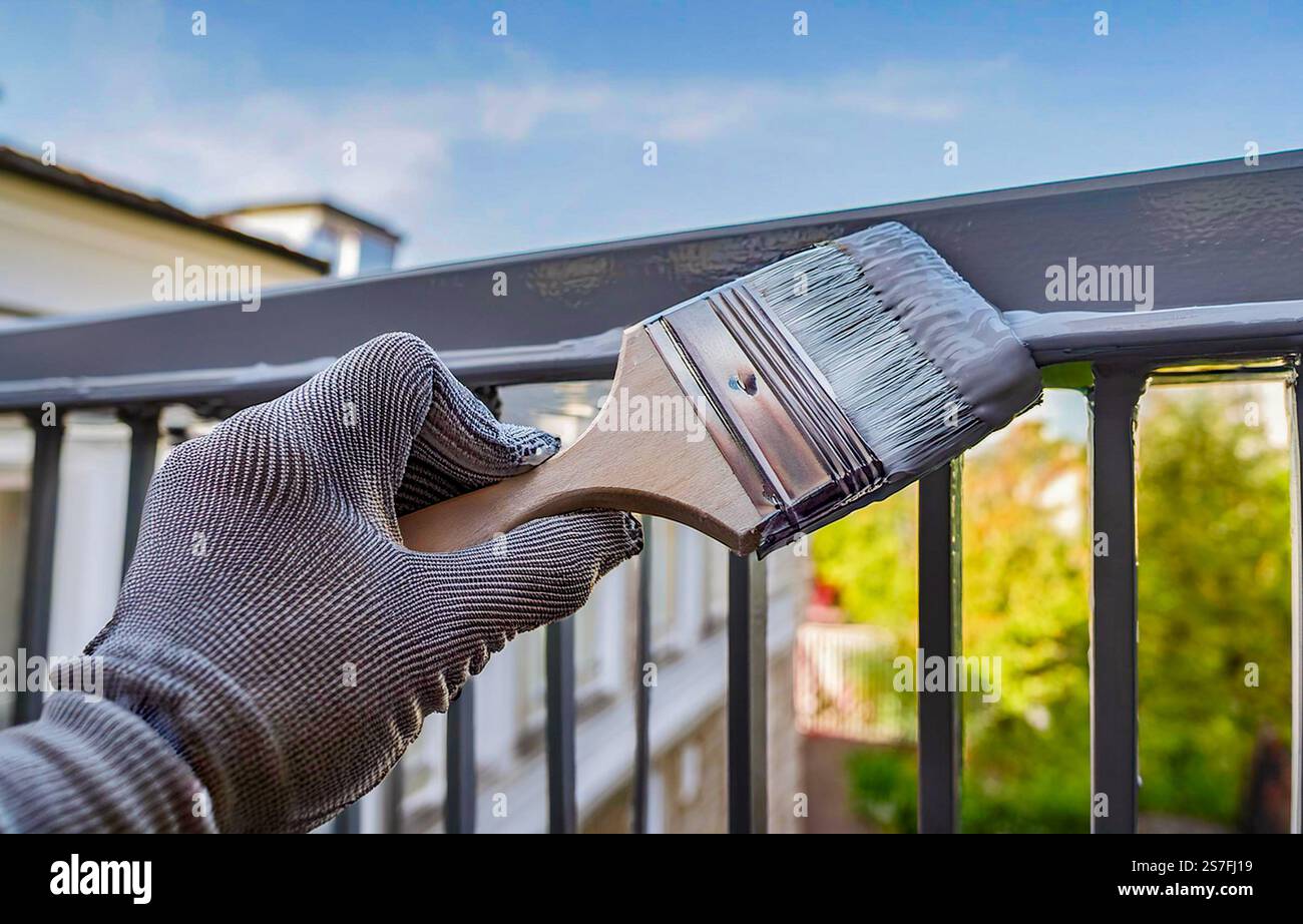 Painter applying gray paint on metal balcony railing using brush Stock ...