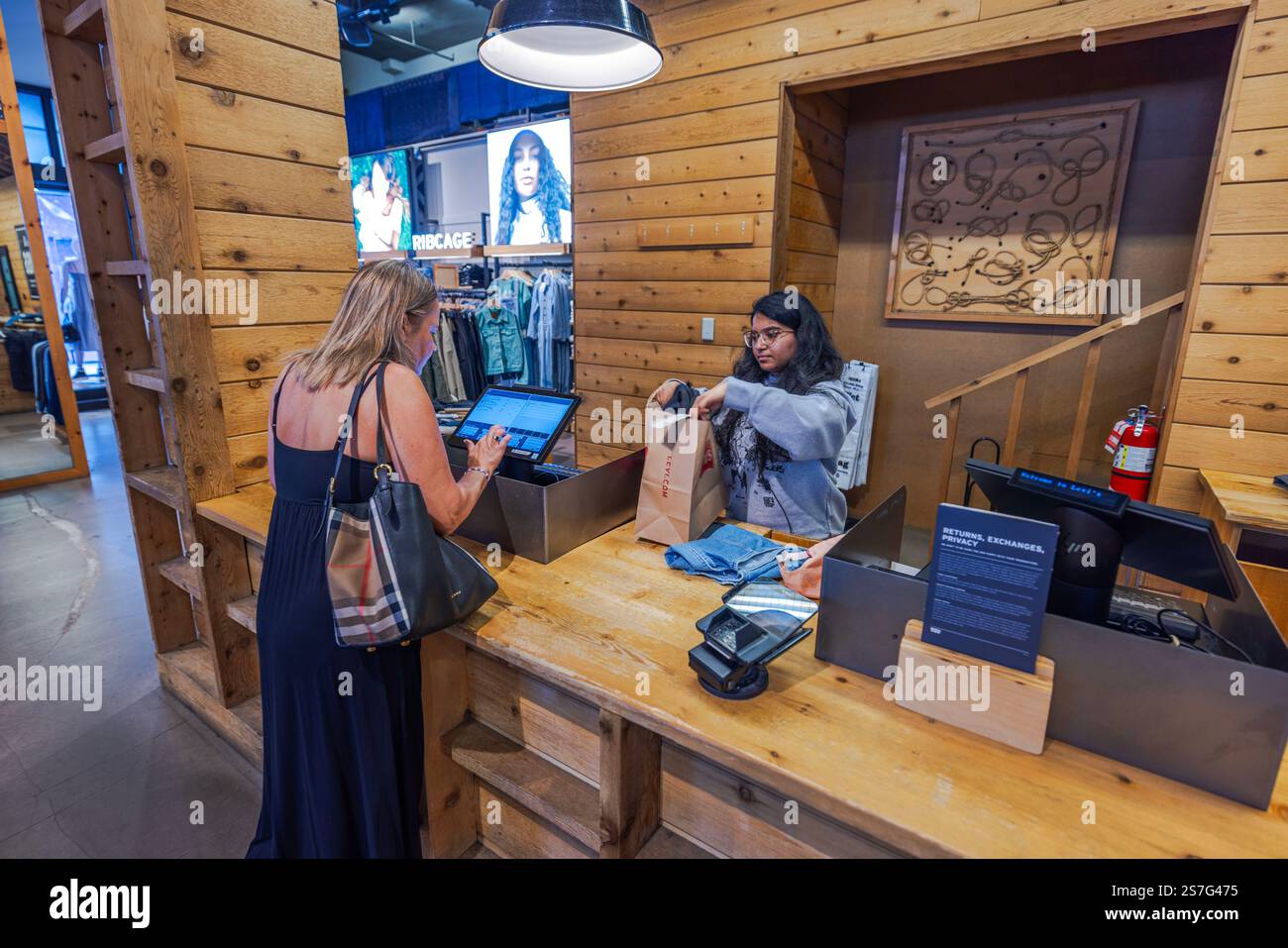 Customer making purchase at Levi's store with cashier packing clothes ...