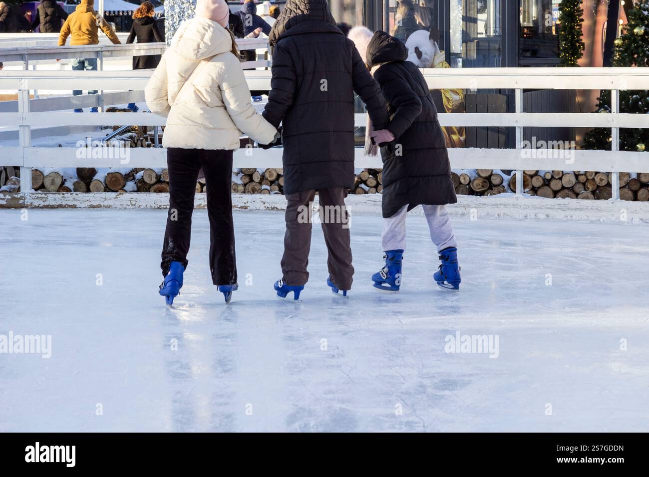Three teenagers holding hands are skating on a rink. The rink is ...