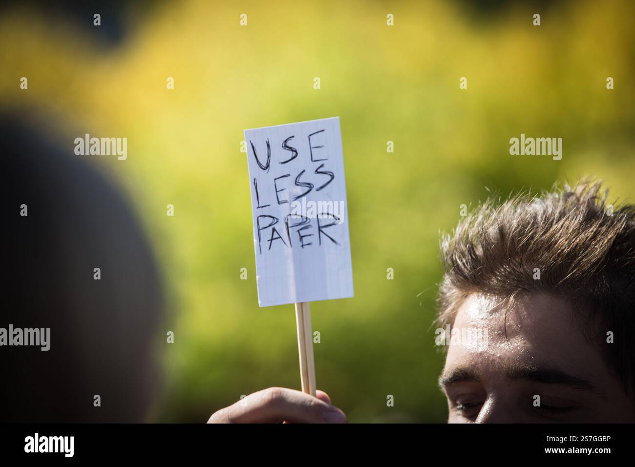 A protestor holds up a handwritten sign reading "USE LESS PAPER ...