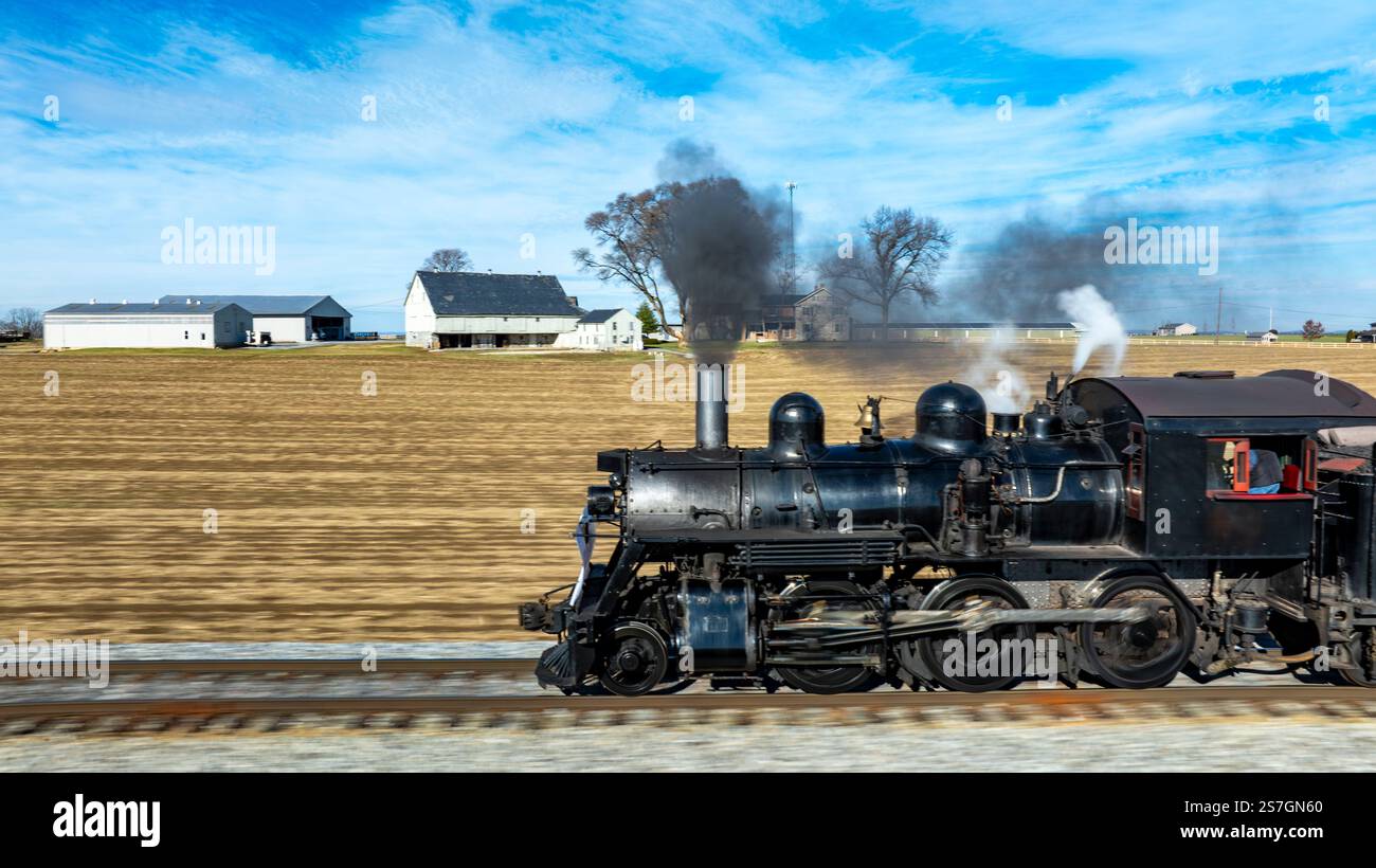 A vintage steam locomotive powers along the tracks, sending plumes of ...