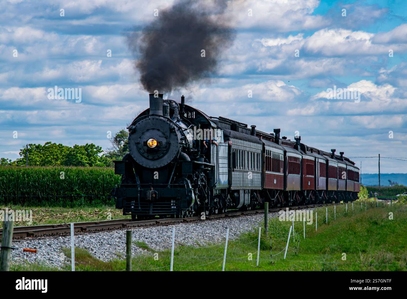 A vintage steam train puffs black smoke as it moves along the railway ...
